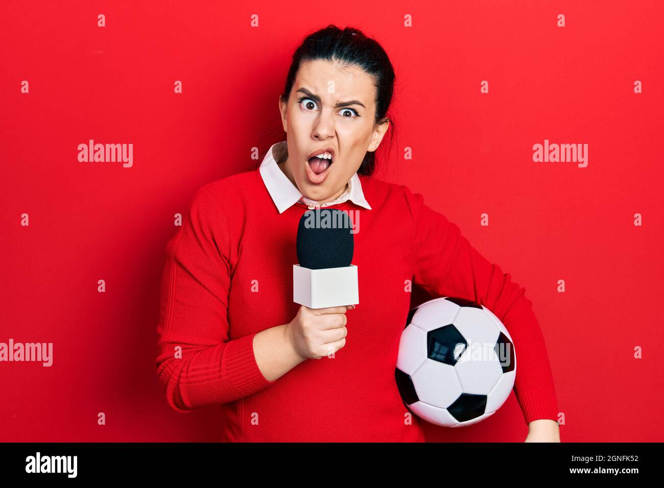 Young hispanic woman holding reporter microphone and soccer ball in ...