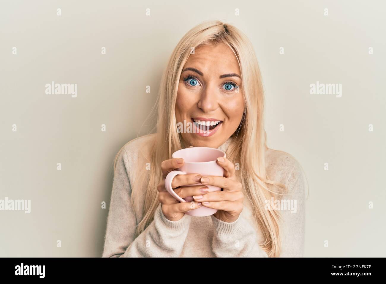 Young blonde woman drinking a cup of coffee celebrating crazy and ...