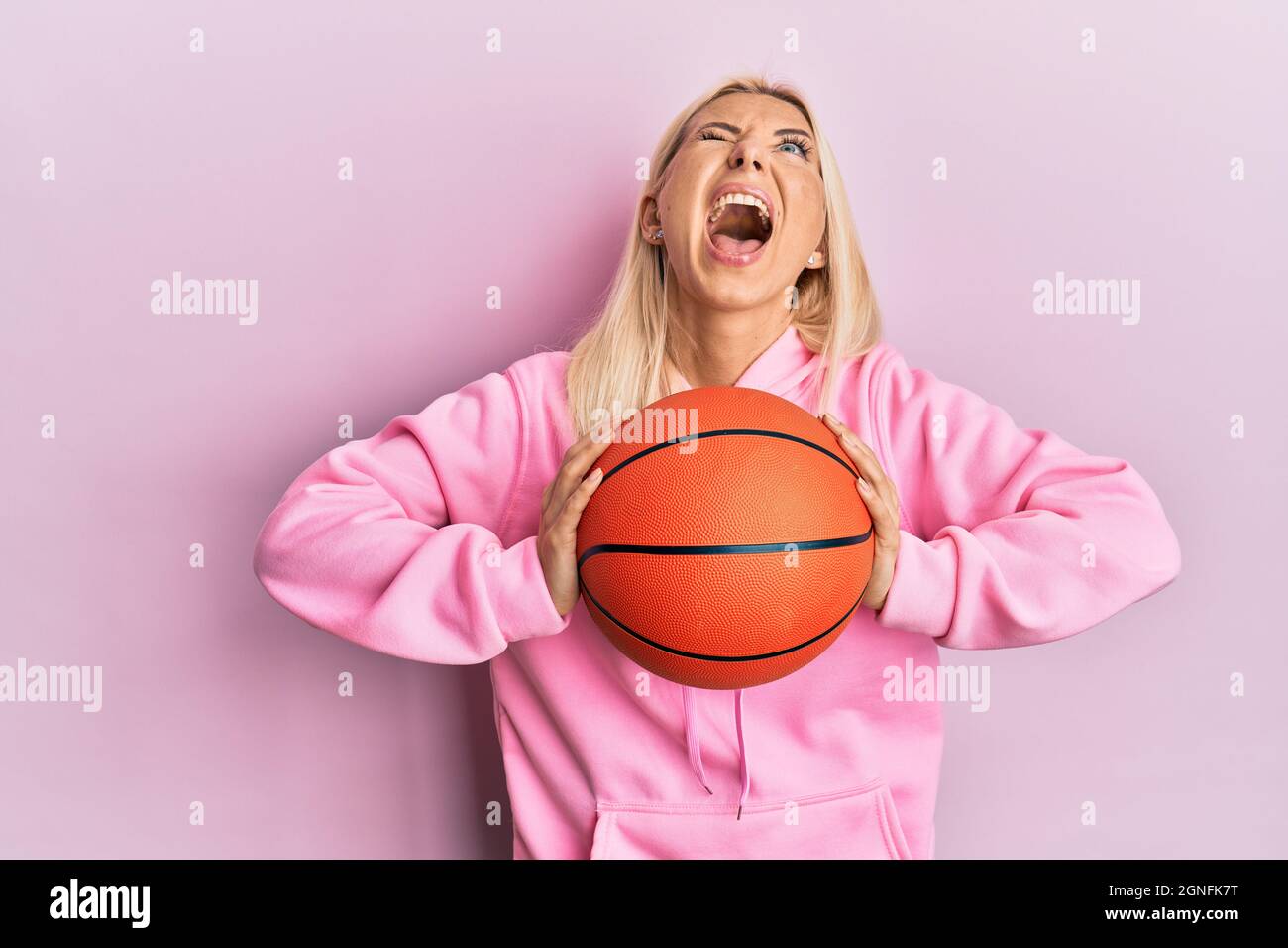 Young blonde woman holding basketball ball angry and mad screaming ...