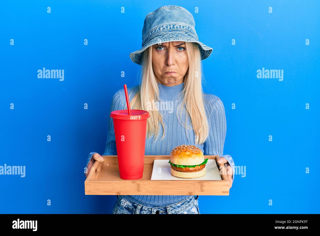 Young blonde woman eating a tasty classic burger and soda depressed and ...