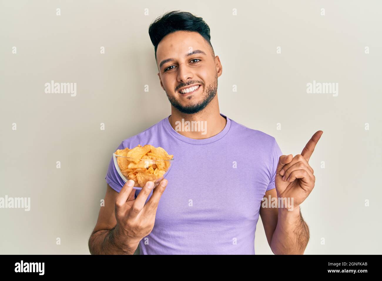 Young arab man holding potato chip smiling happy pointing with hand and ...
