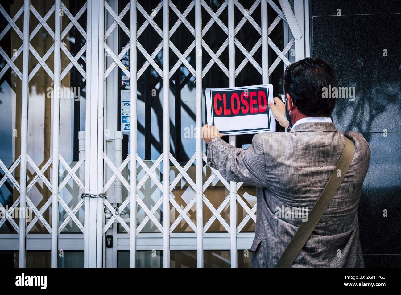 Rear view of businessman putting closed sign on display on locked shop ...