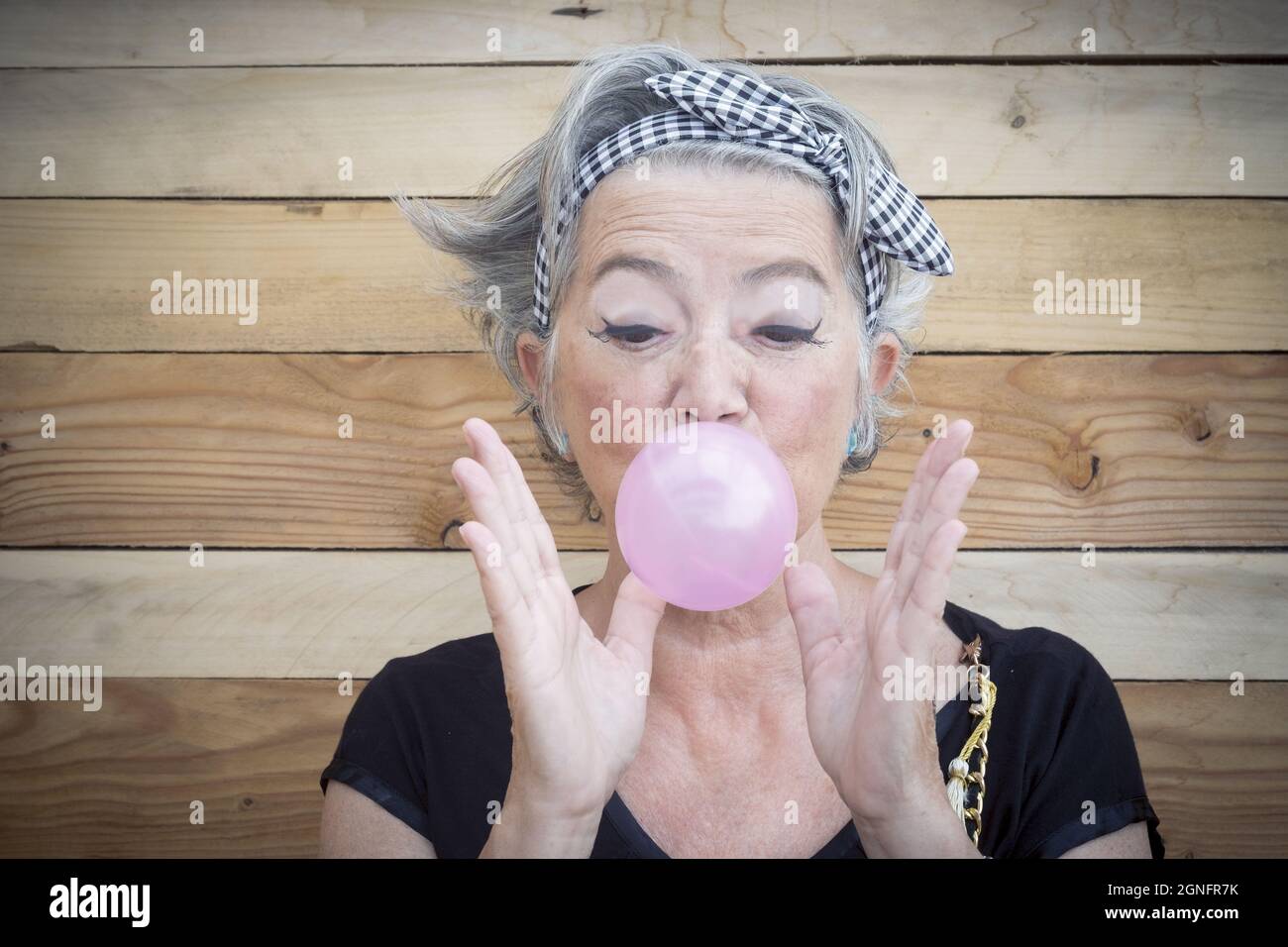 Portrait of senior woman in t shirt and bandanna showing balloon of ...