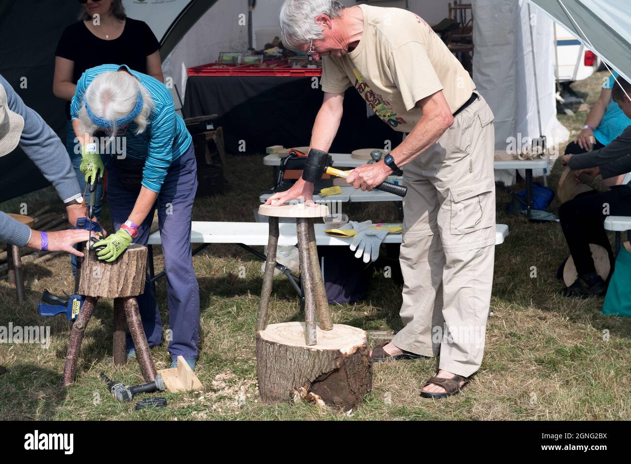 Two elderly couple making hand made stools at an open air woodcraft ...