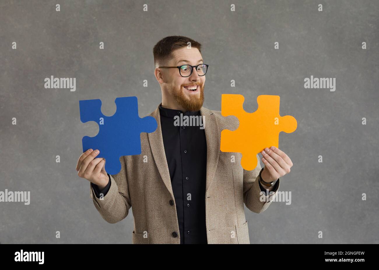 Funny smiling male office worker, makes up two colored puzzle pieces ...