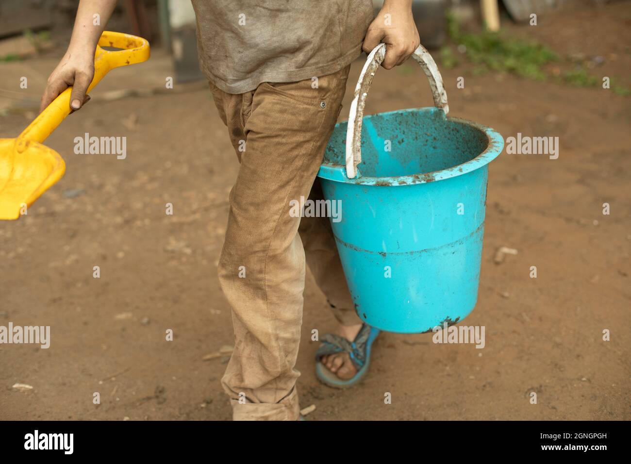 The child is holding a bucket. Blue bucket in hand. The boy plays with ...