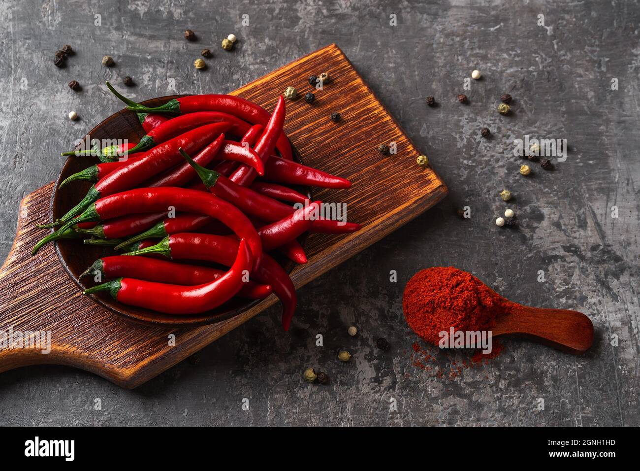 Ground chili pepper in a wooden spoon near fresh red hot chilli peppers ...
