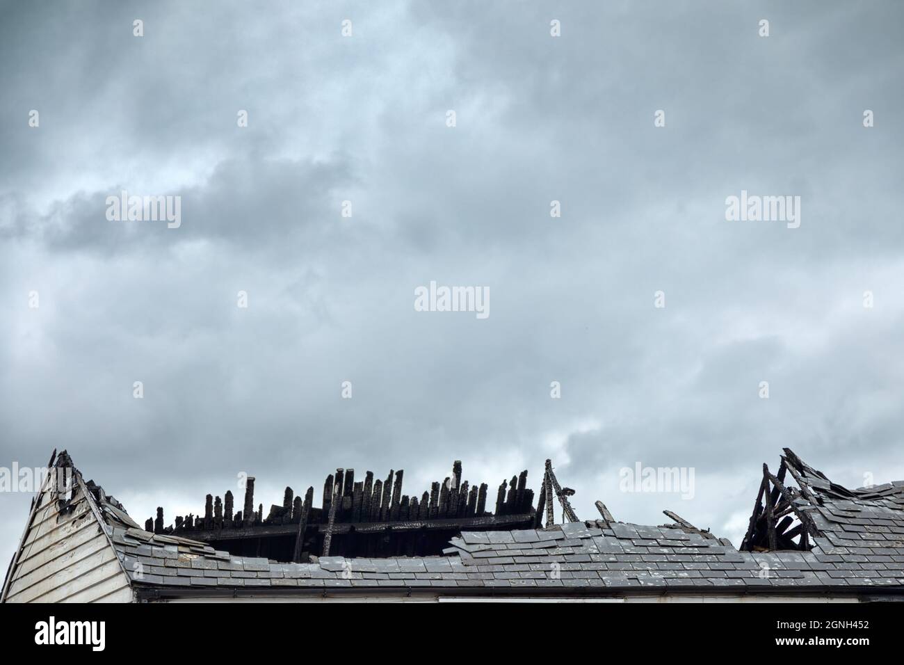 Grey cloudy sky above fire damaged roof with blackened wooden beams and ...