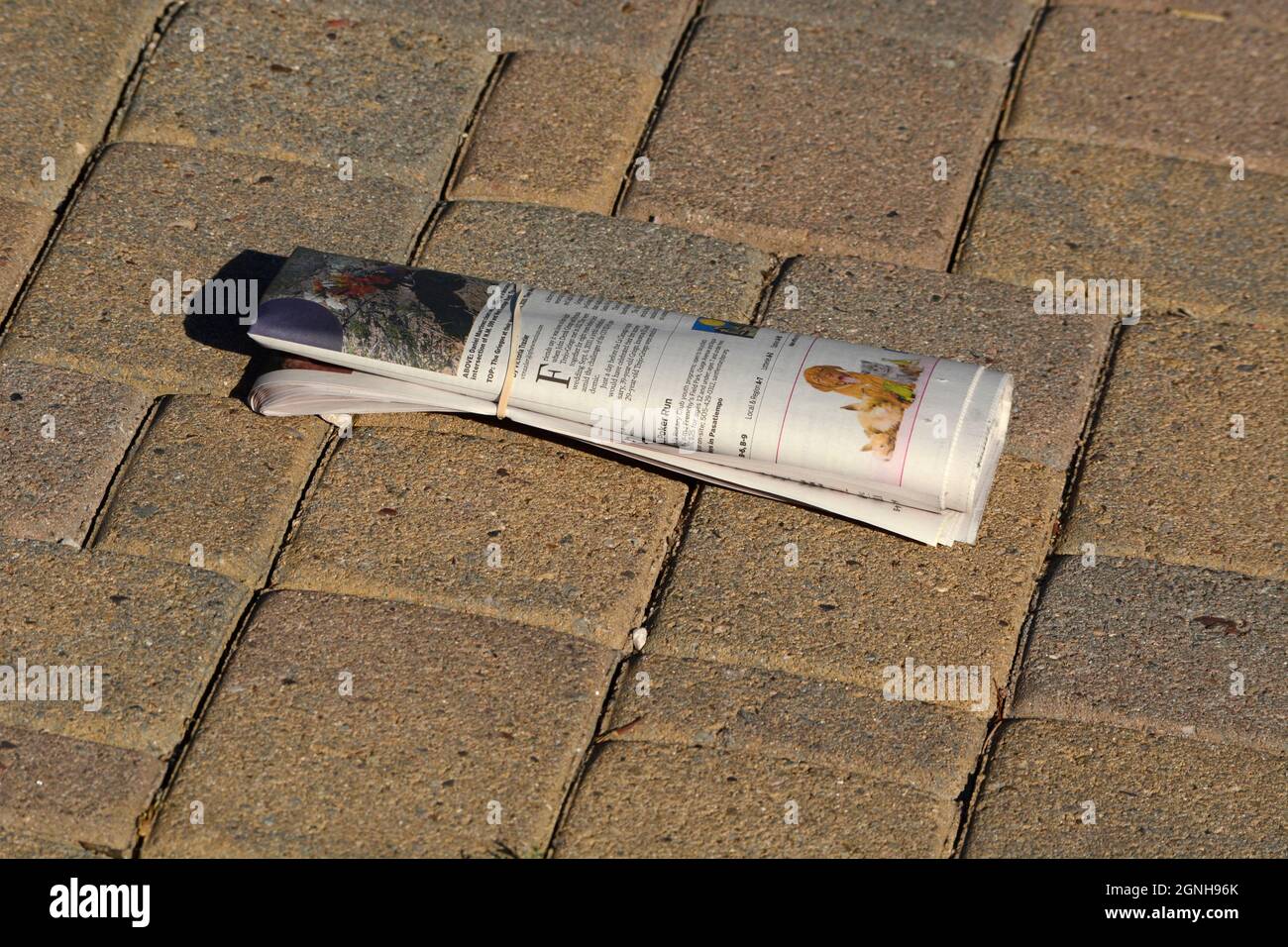 A home-delivered local daily newspaper in the driveway of a home in ...