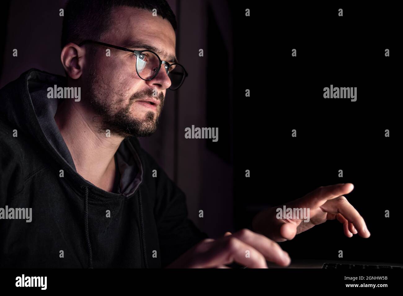 A man stares intently at a computer screen in the dark at night, copy ...