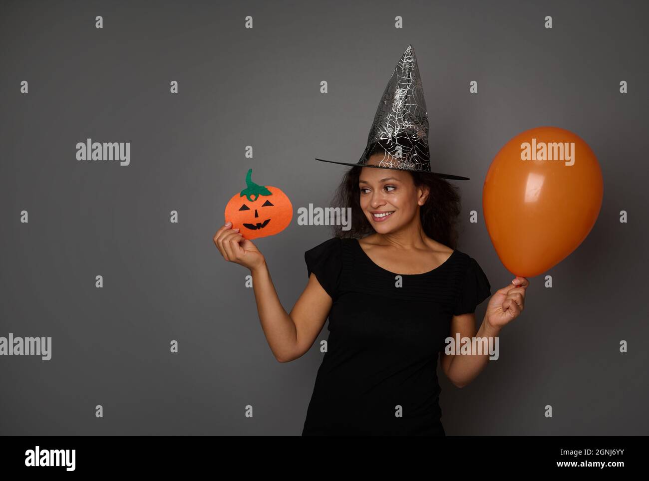 Cheerful woman wearing a wizard hat, dressed in black attire, holding a ...