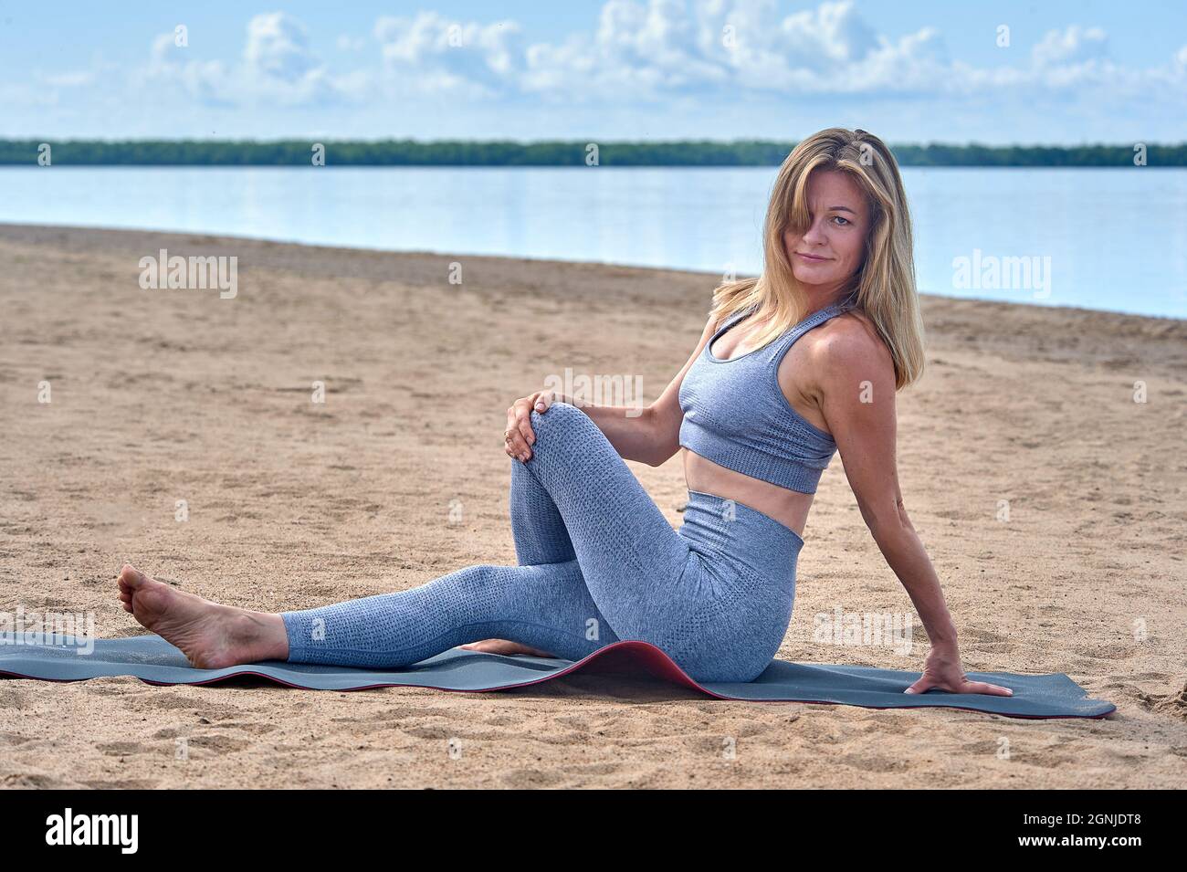 A woman does yoga on a sandy beach against the background of a river ...