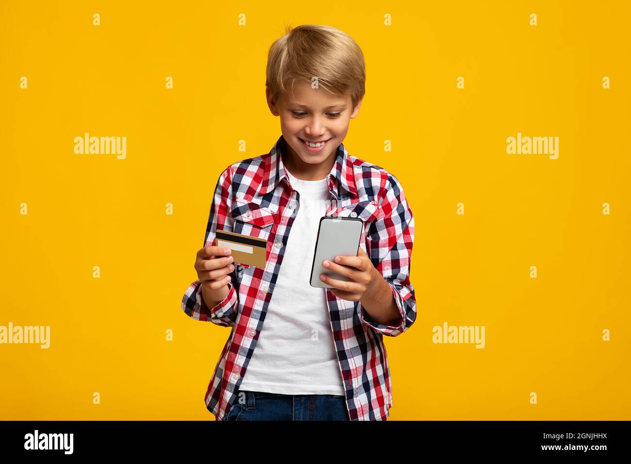 Cheerful caucasian teenage boy holding credit card and phone paying and ...