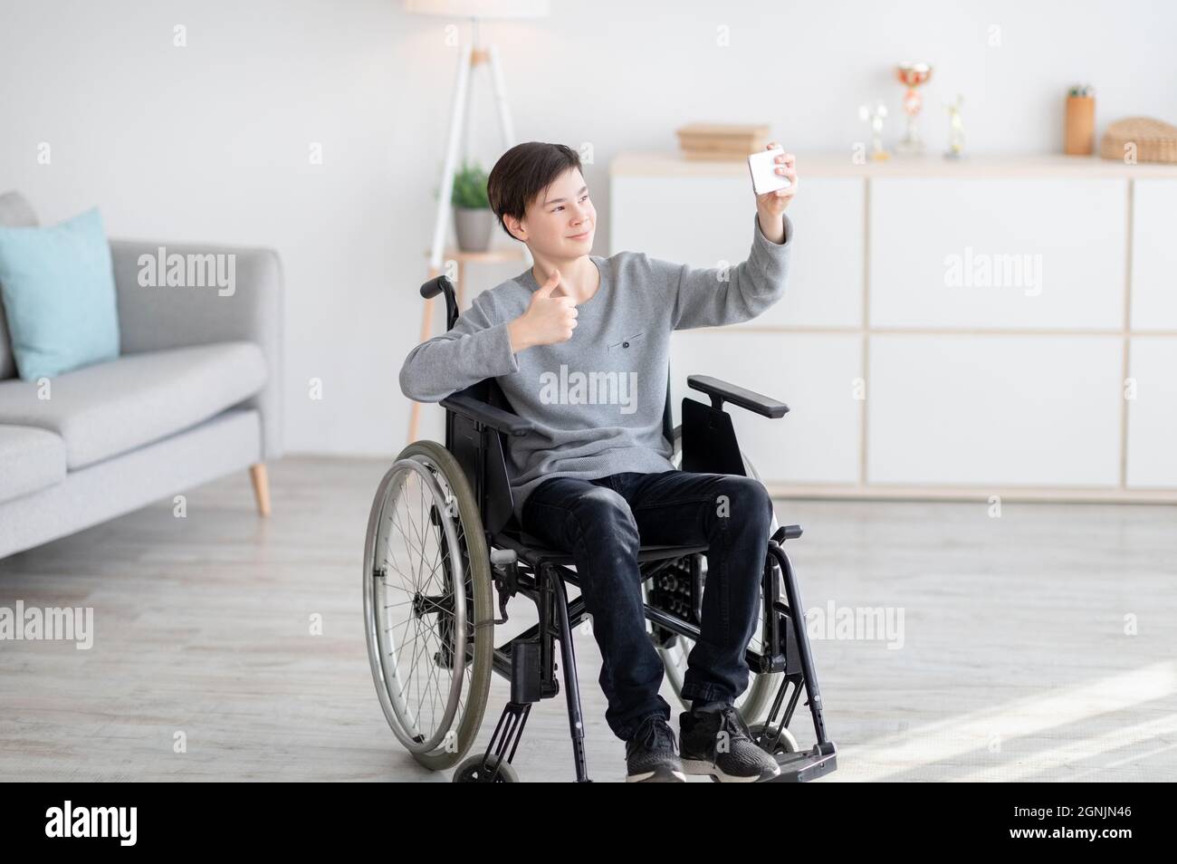 Joyful disabled teenager in wheelchair posing for selfie, using ...