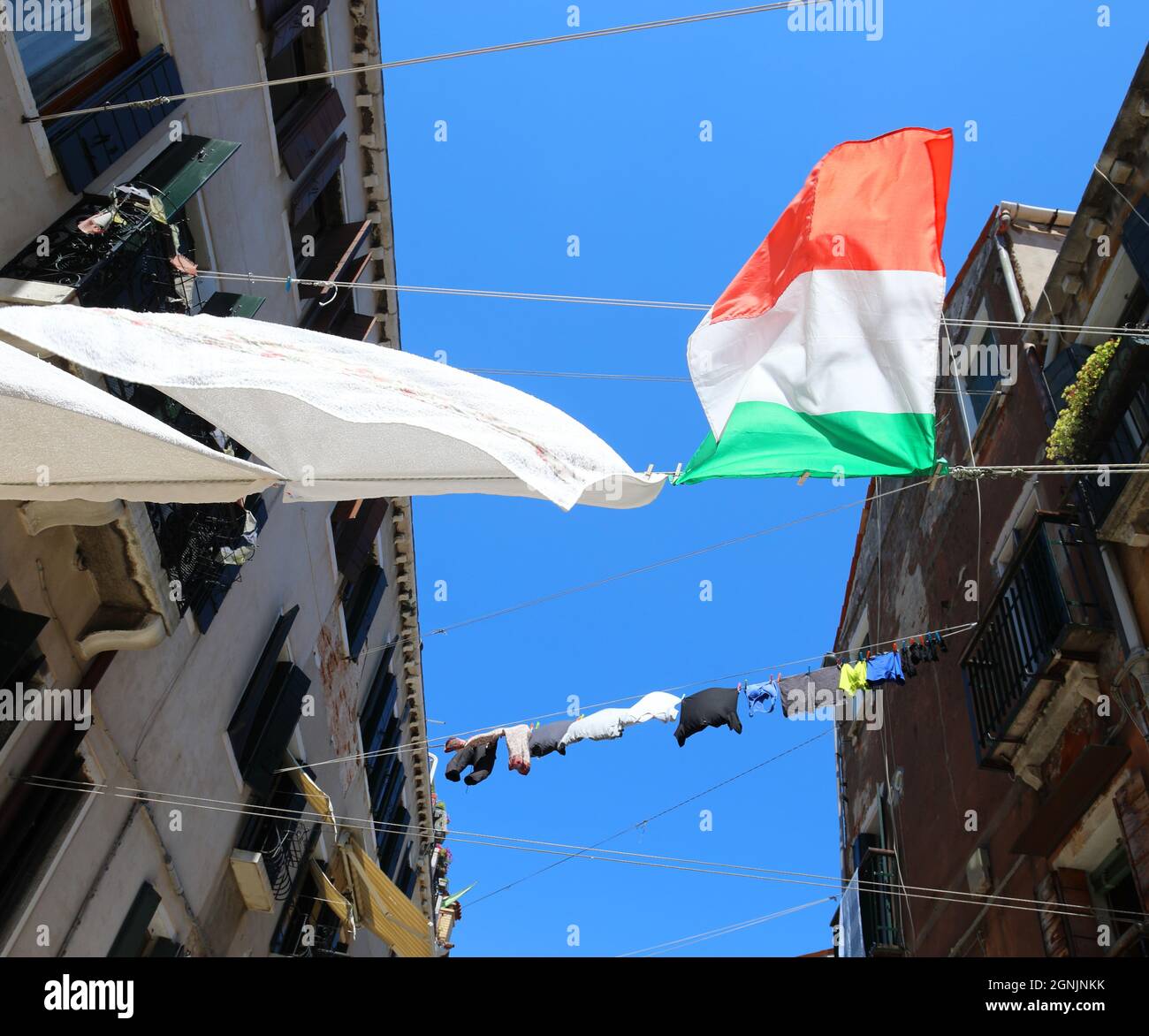 many clothes hanging is a large Italian flag in the alley between the ...
