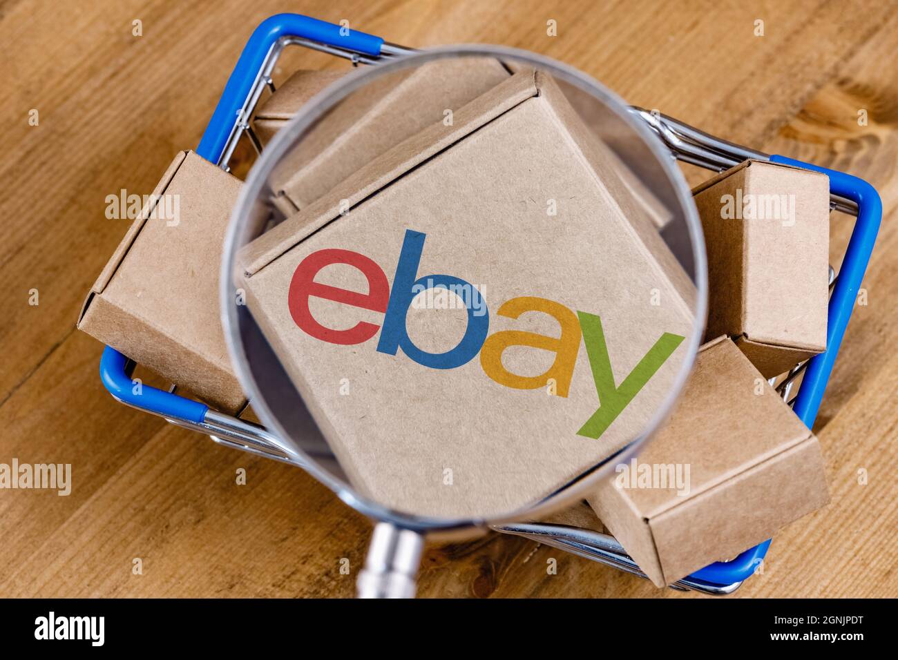 Ebay logo on a box under a magnifying glass. Boxes in the shopping cart ...