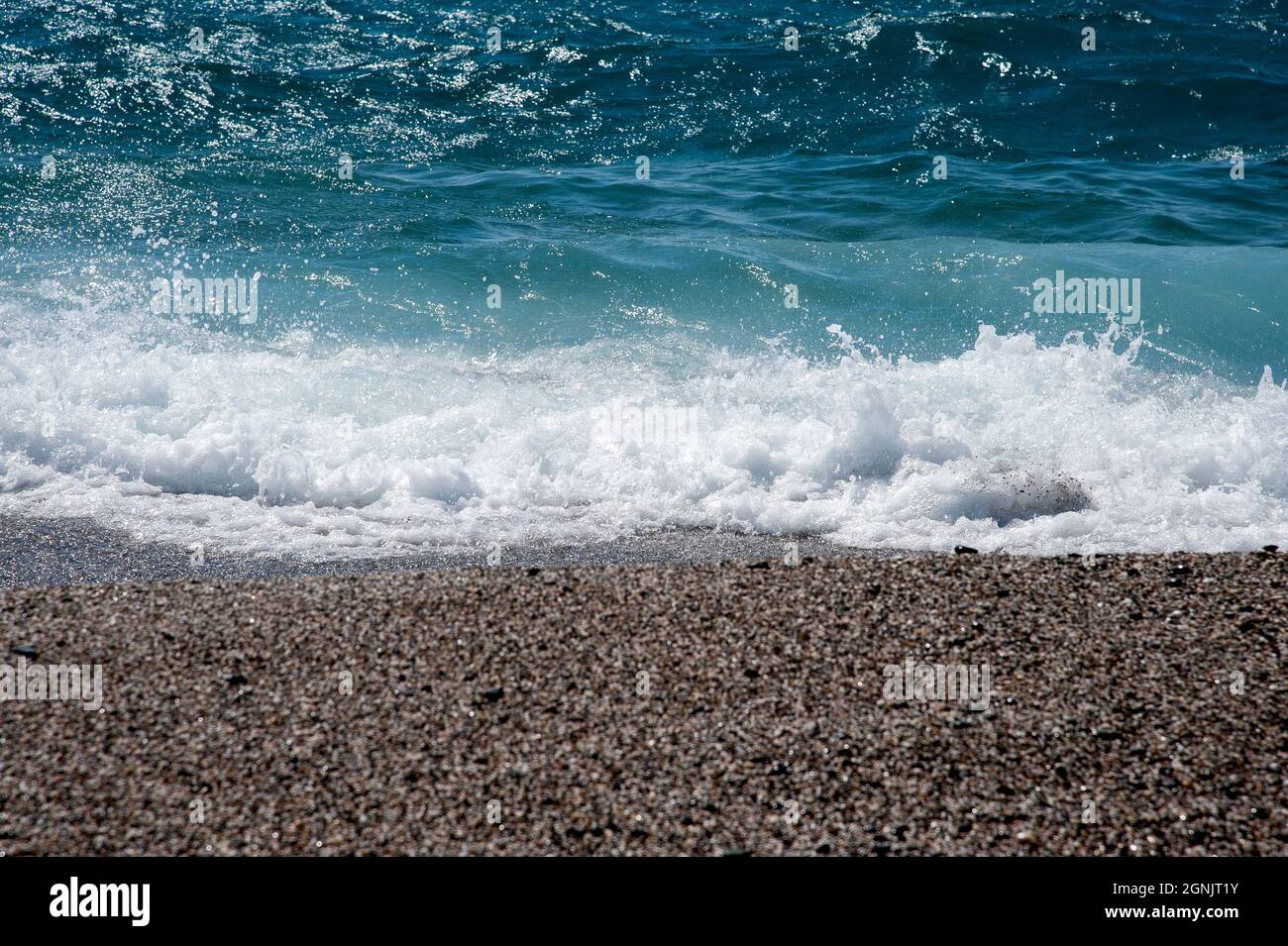 Splashing waves on a sunny beach in Greece Stock Photo - Alamy
