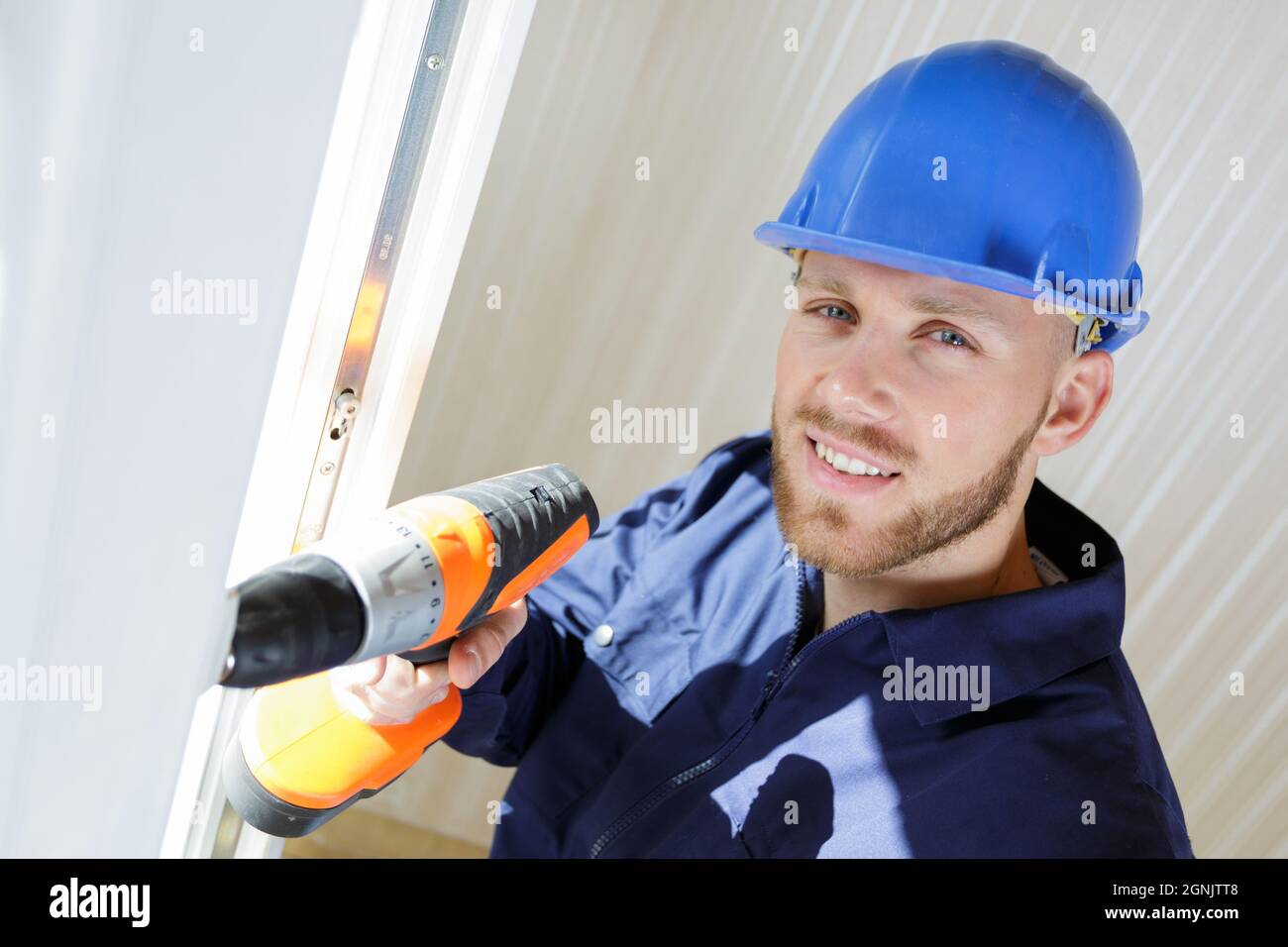 male builder using a drill to install a window Stock Photo - Alamy