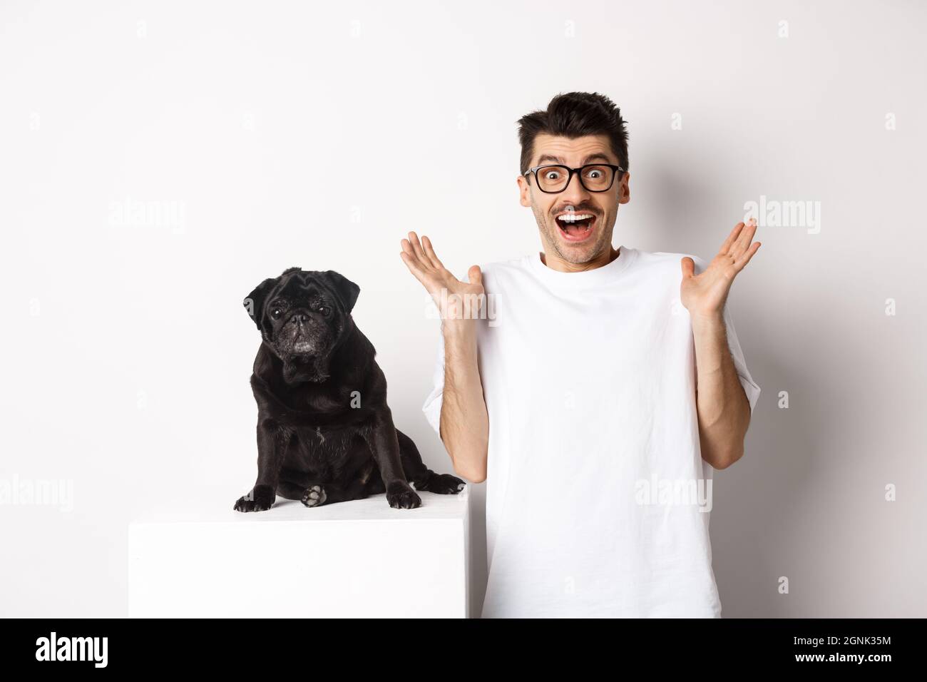 Cheerful young man in glasses standing with his pet, rejoicing and ...