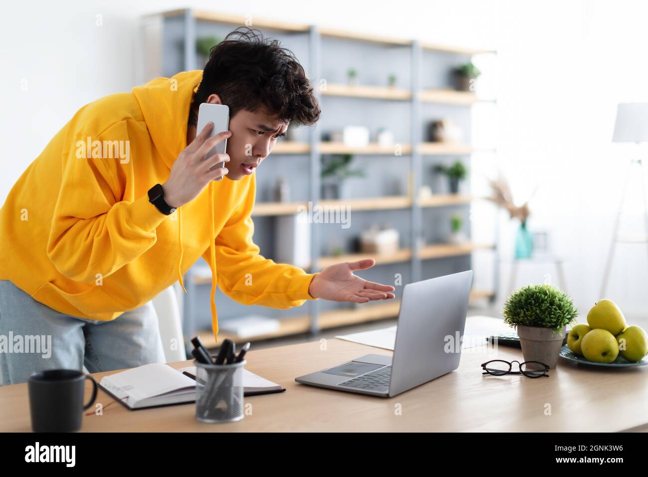 Confused asian man talking on mobile phone using laptop Stock Photo - Alamy