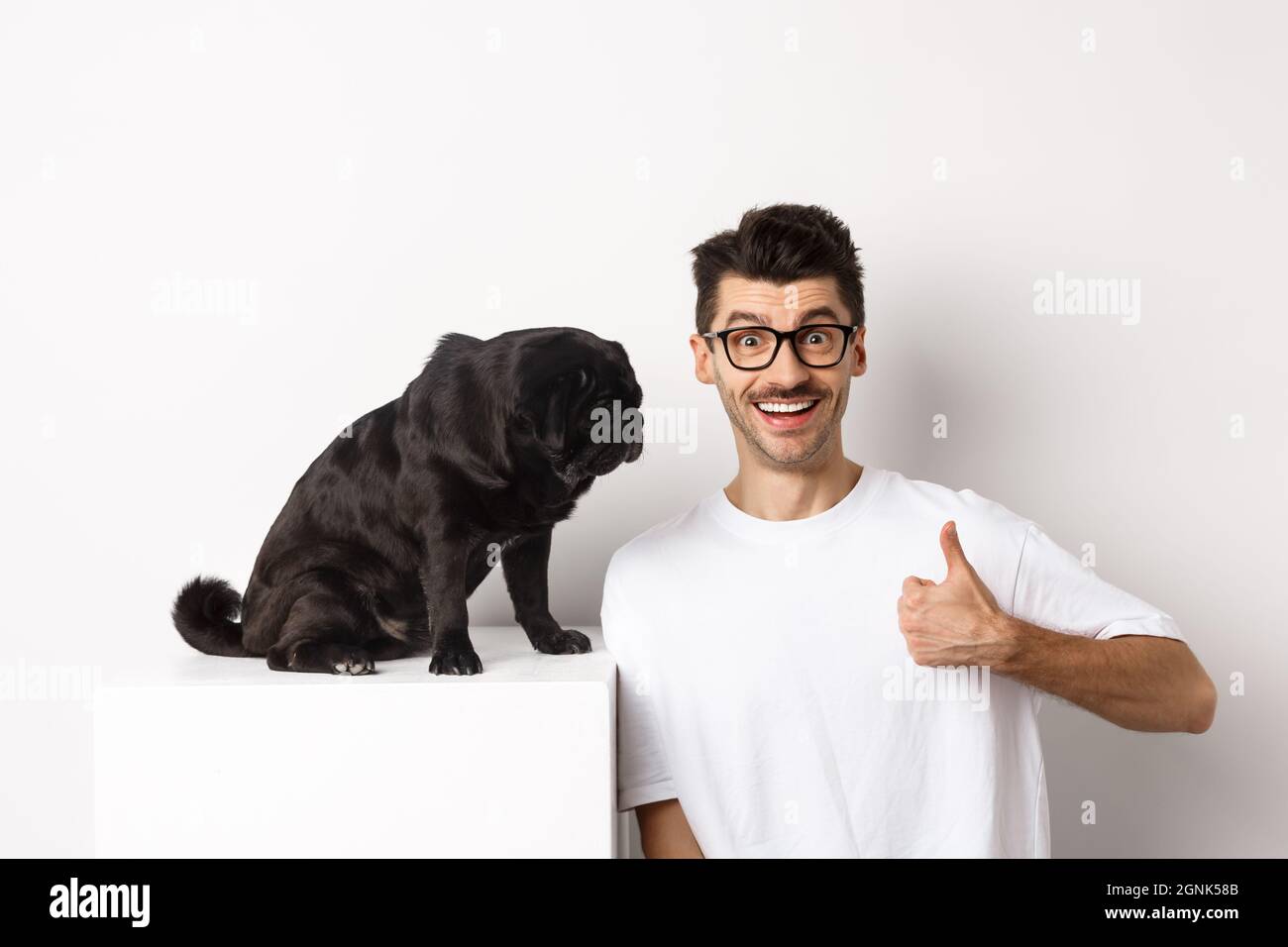 Image of happy and satisfied young man sitting near pug dog and showing ...