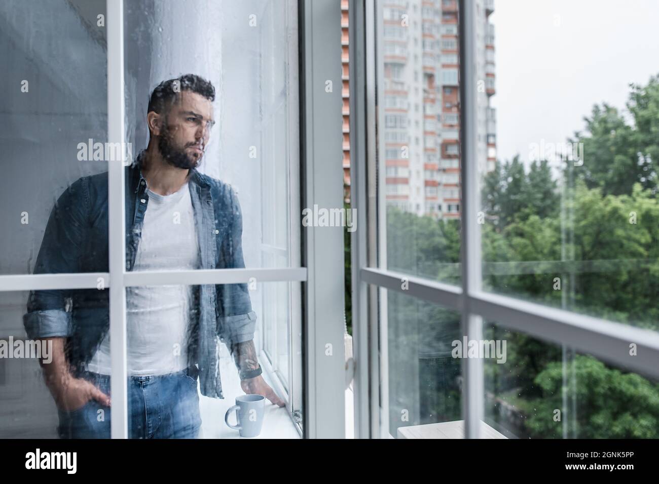Depressed sad man looking through window, hoping for end of pandemic ...