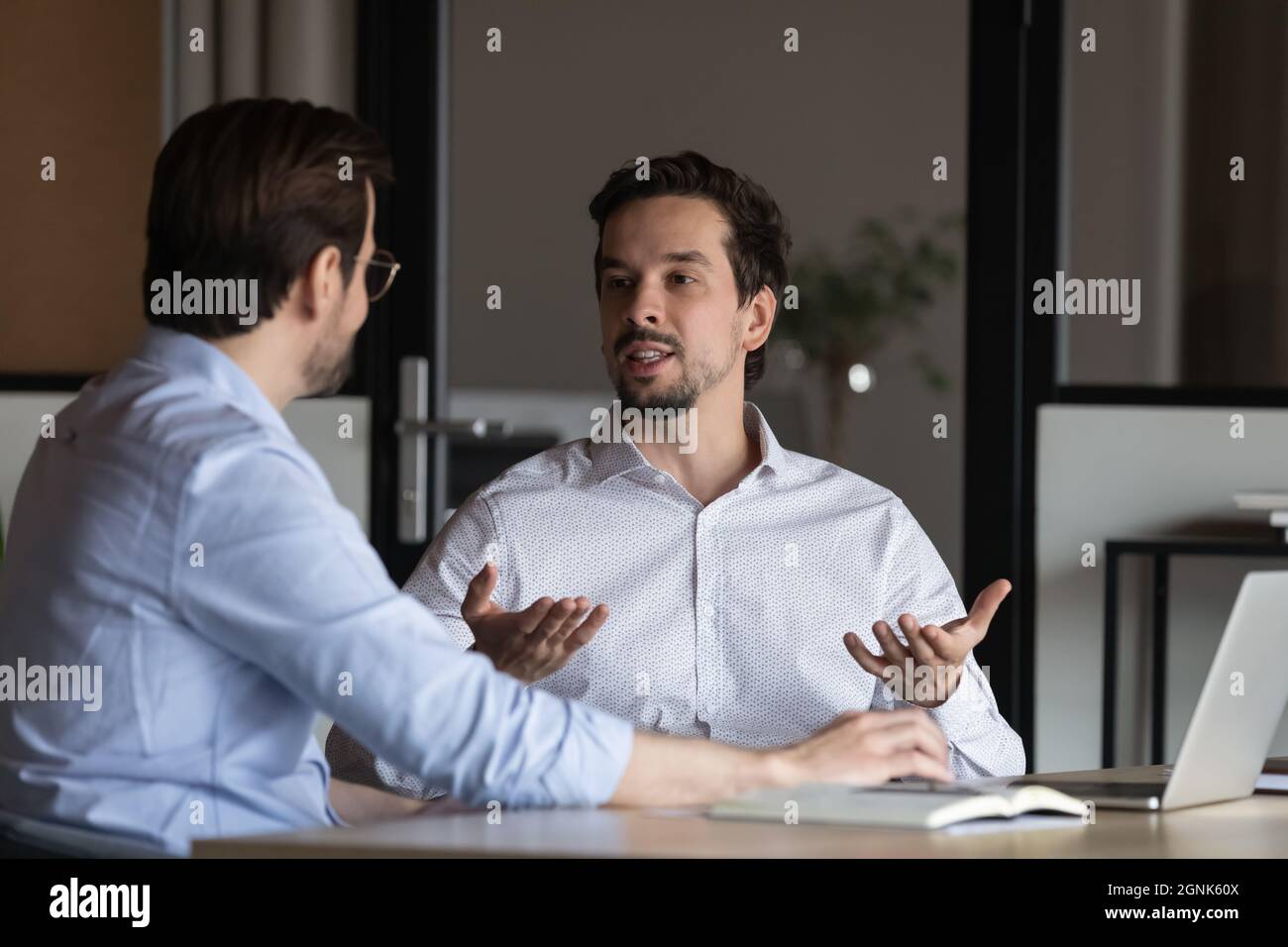 Two office employees meeting and working at workplace laptop, talking ...