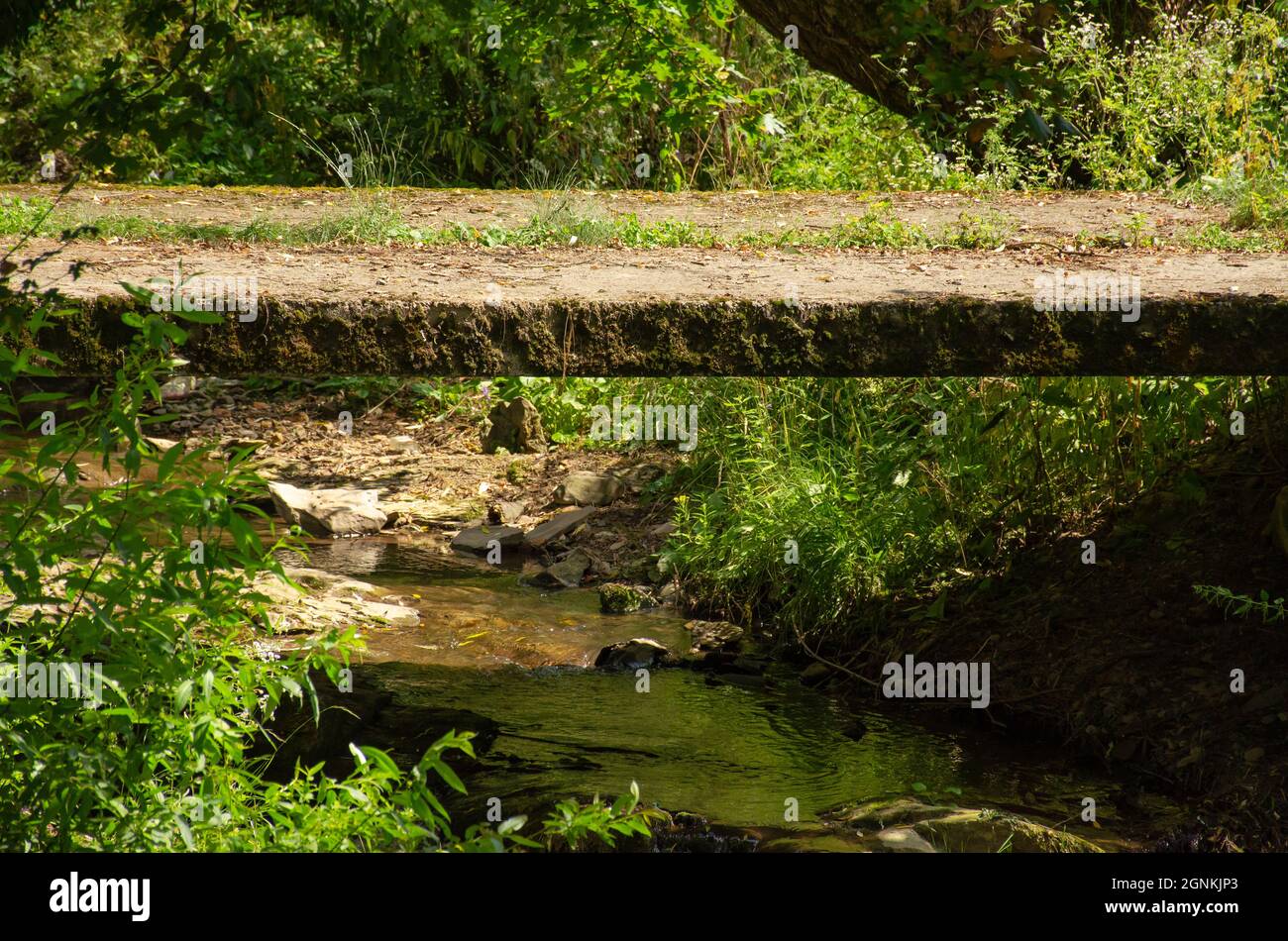 Rural small concrete bridge over small shallow stream and rocky ...