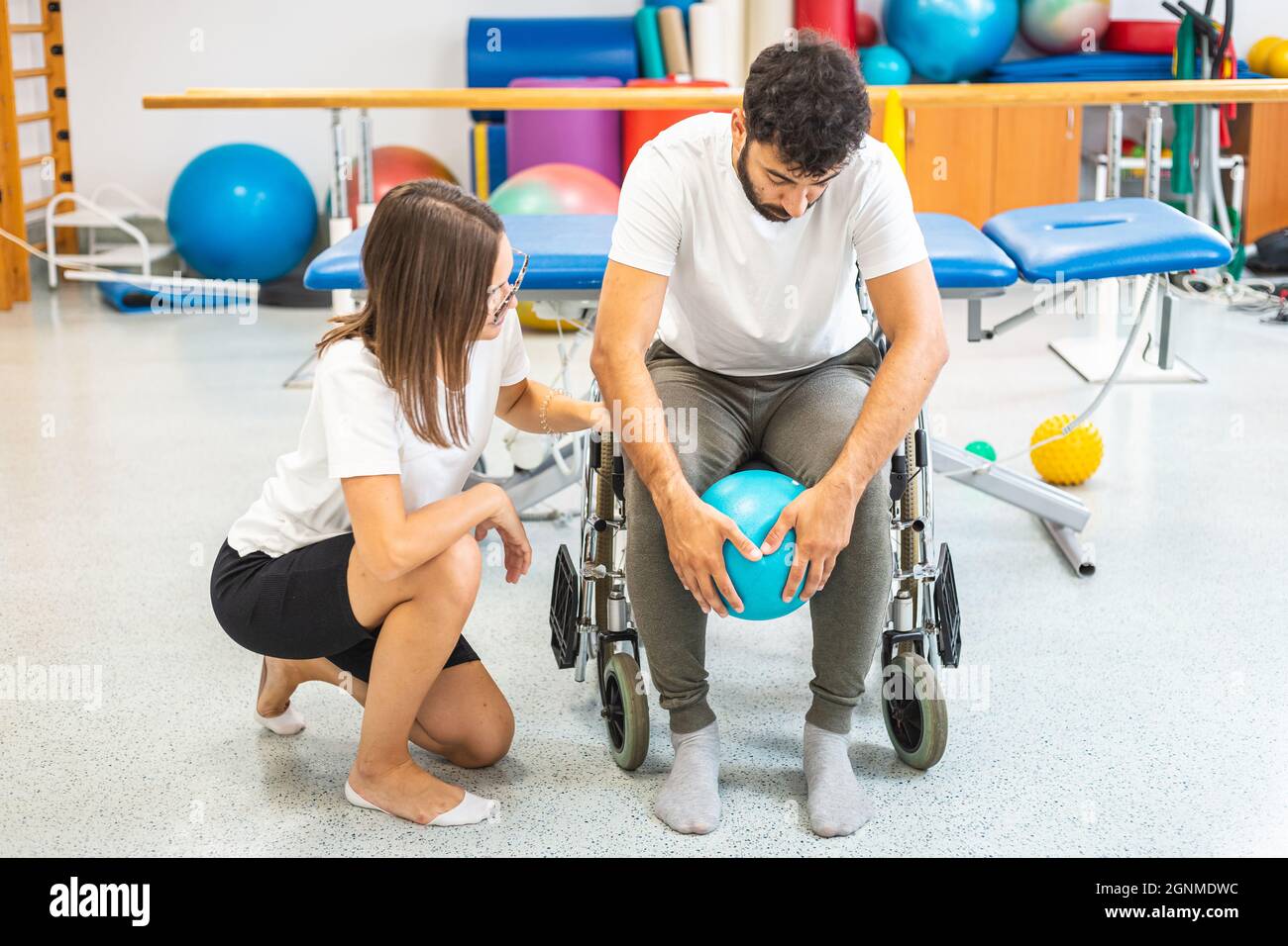 Disabled man seated in a wheelchair, doing an exercise with a smaller ...