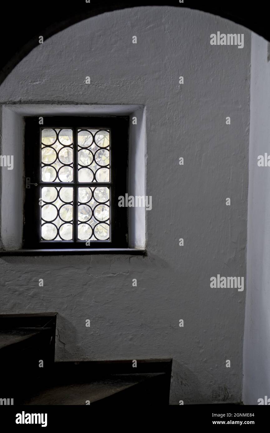 A grayscale shot of an old small window near a staircase in a building ...
