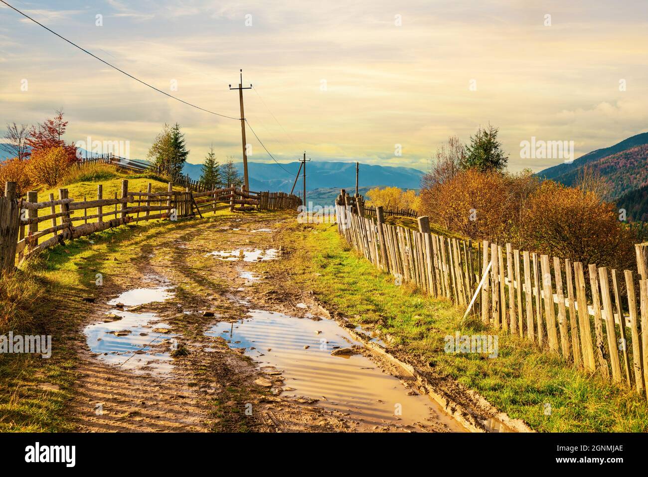 A path along the ridge of a hill with a large puddle and an old fence ...