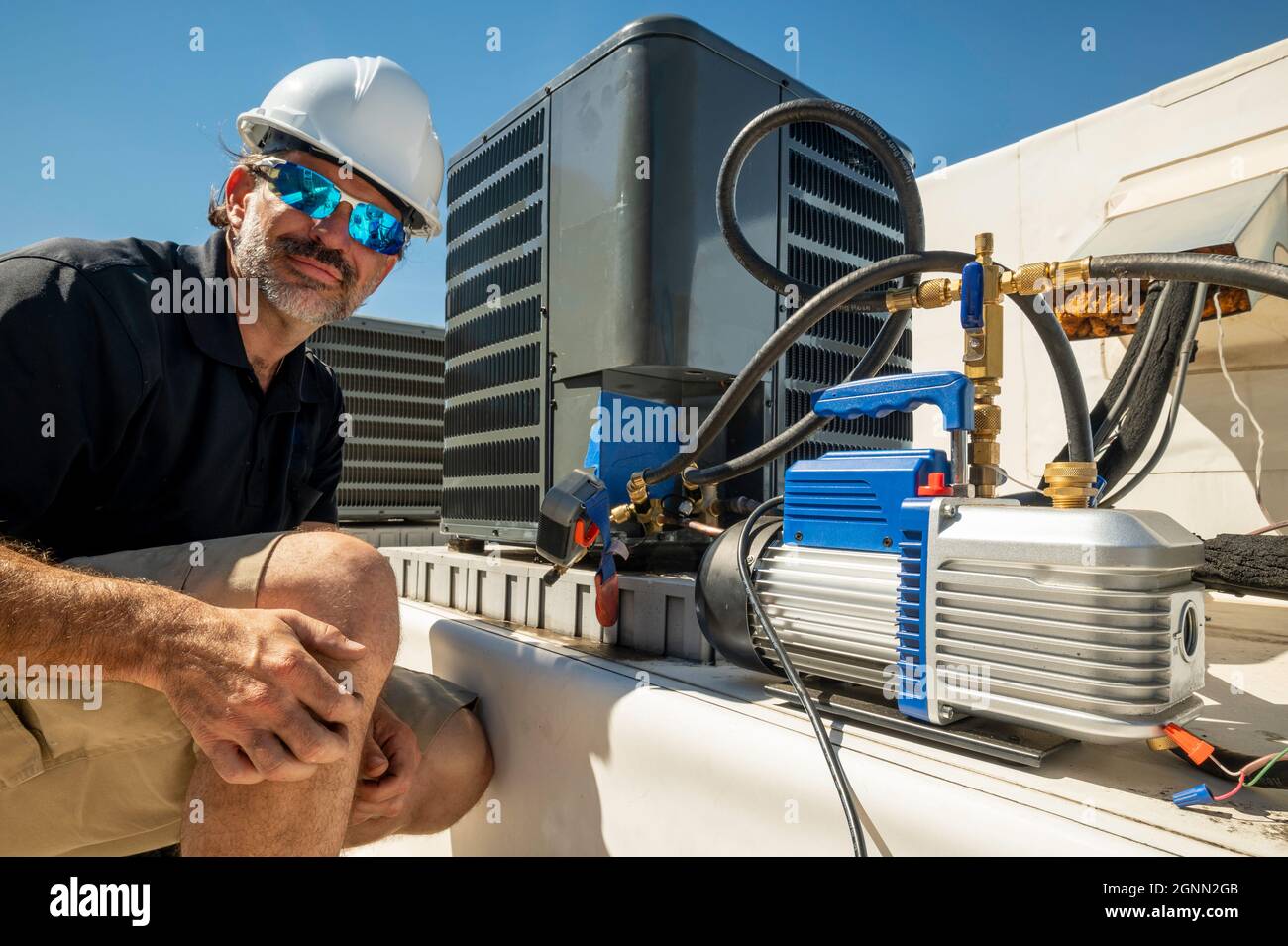 HVAC technician looking at camera, next to evacuation tools for air ...
