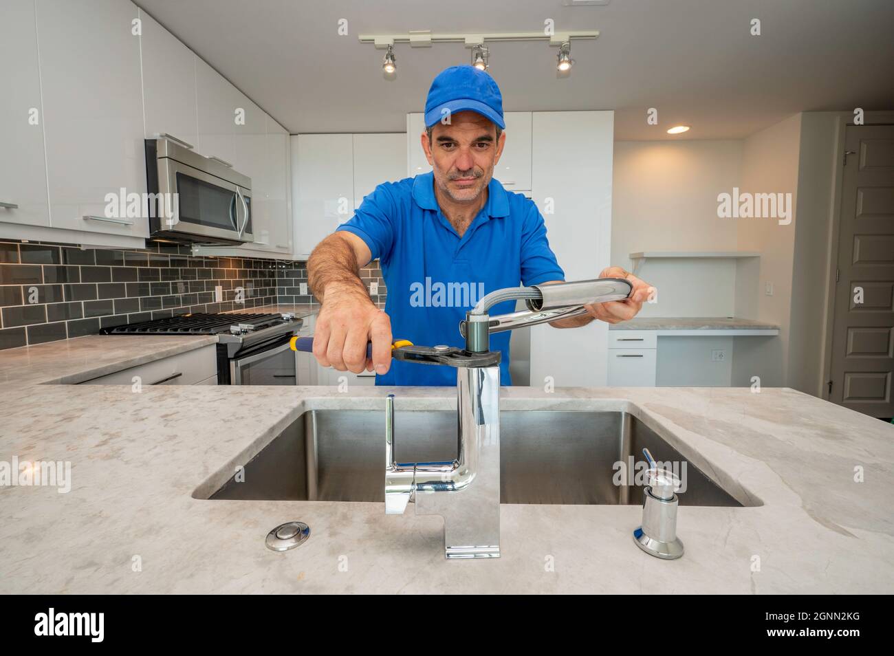 Plumber in blue uniform using pliers to repair or install a kitchen ...