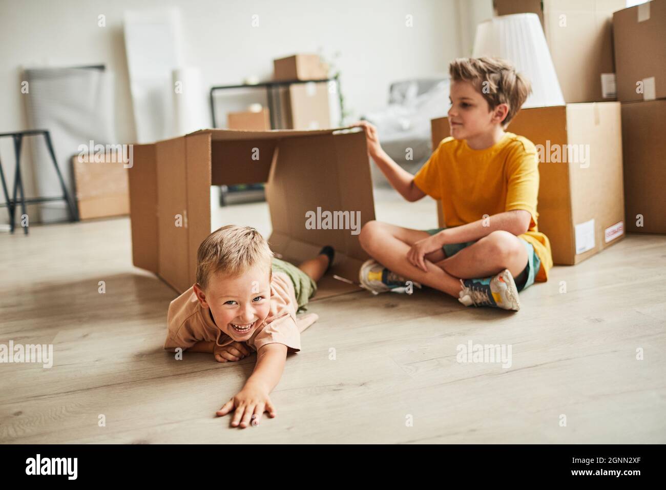 Full length portrait of two brothers playing with cardboard box while ...