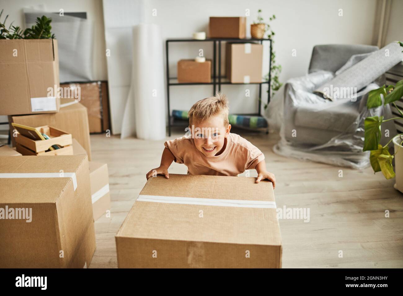 Portrait of smiling little boy moving cardboard box while family ...