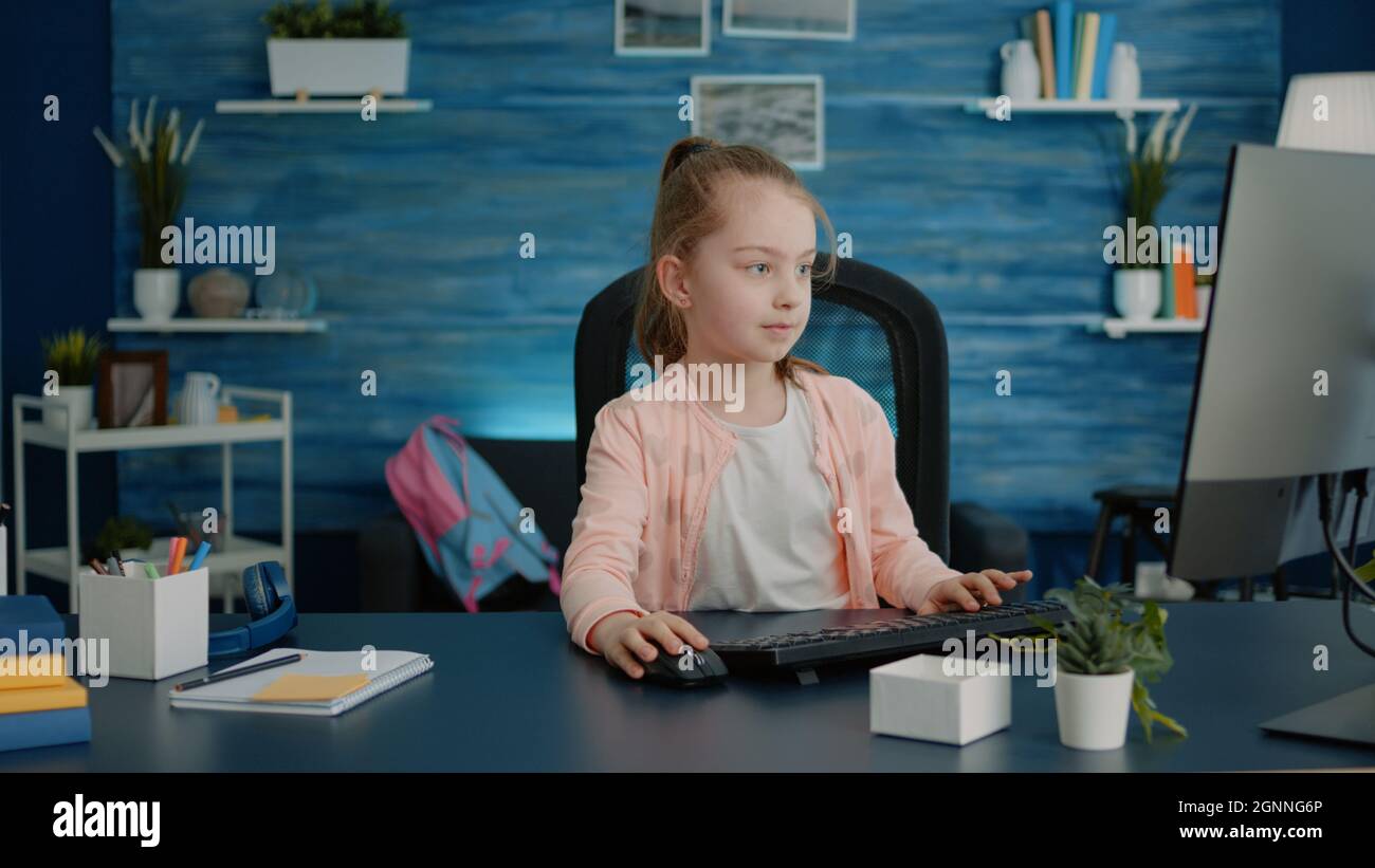 Elementary school child using computer and keyboard at desk for homework and learning. Little ...