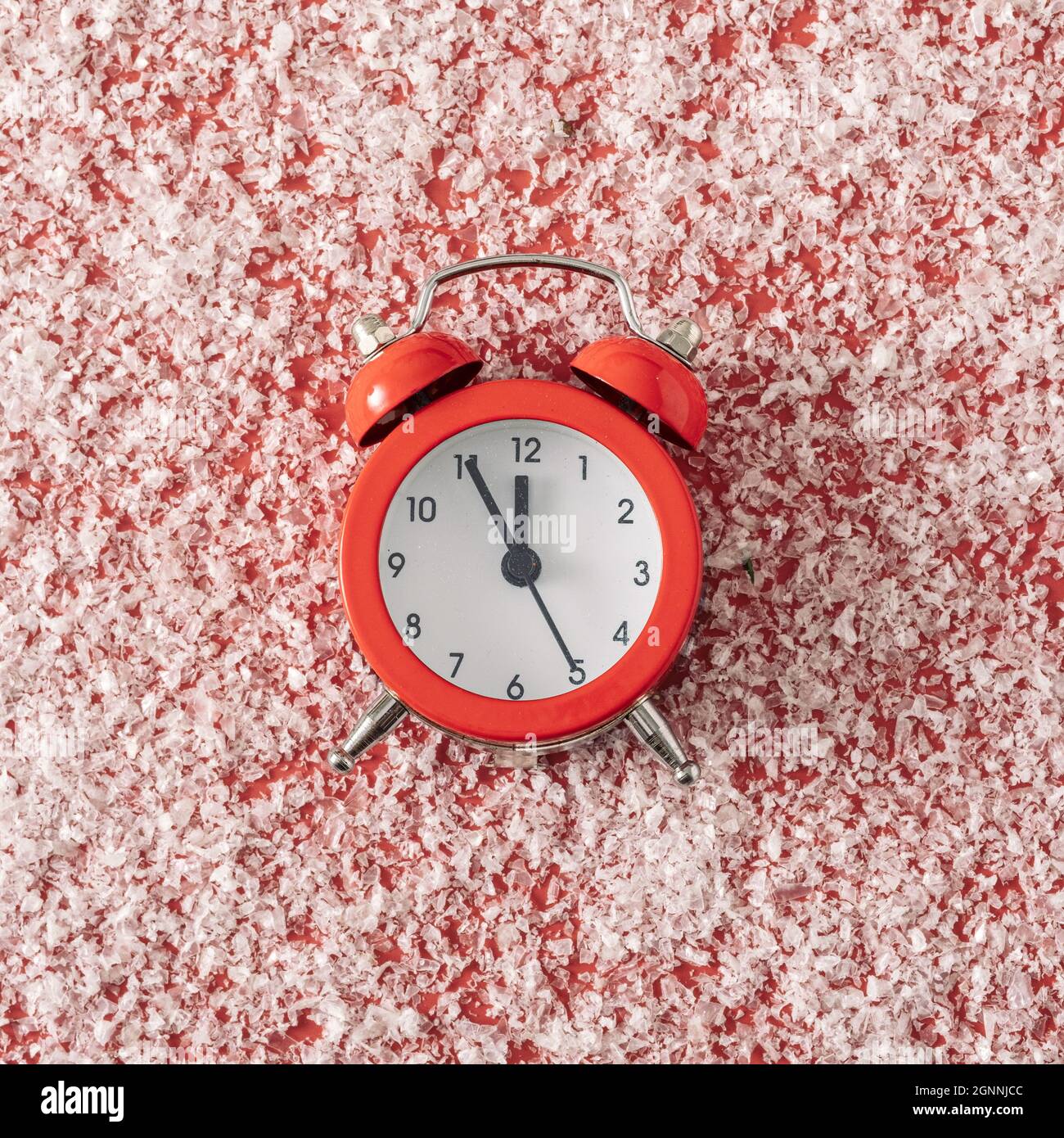 Classic retro alarm clock on a red background with white snow. Minimal ...