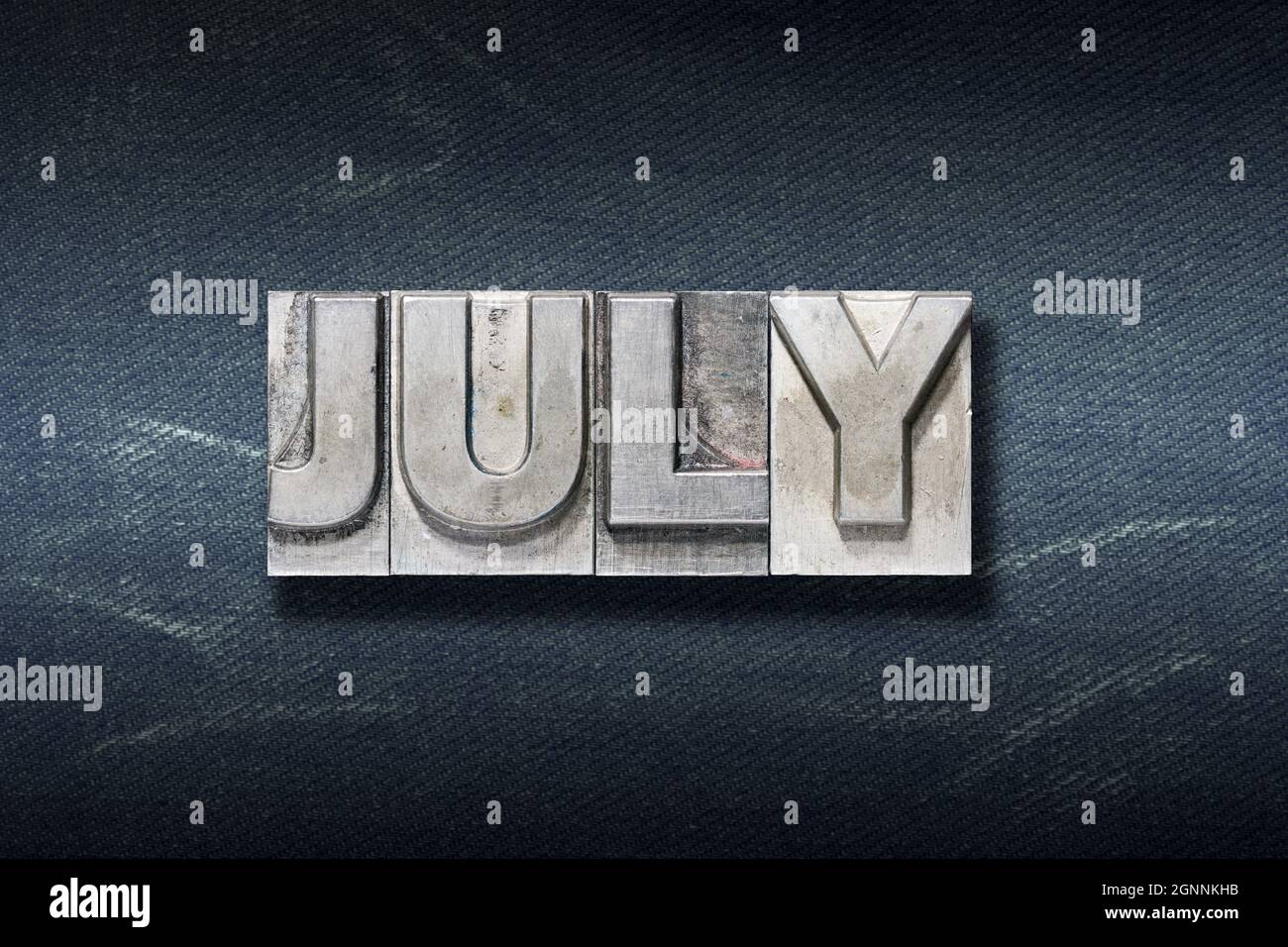 July word made from metallic letterpress on dark jeans background Stock ...
