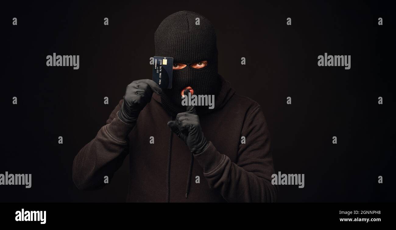 Thief in black balaclava holding black credit card. Banking and non ...