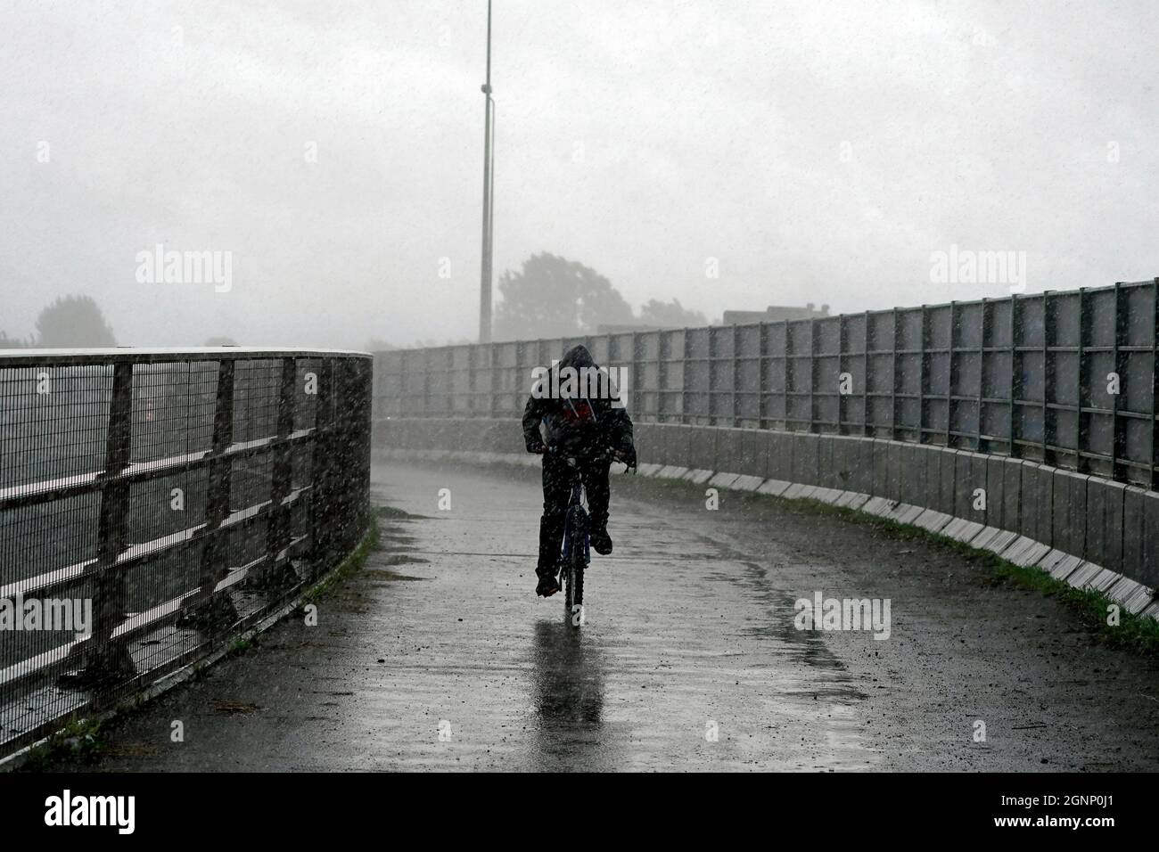 A cyclist crosses a bridge over the M25 motorway in the pouring rain ...