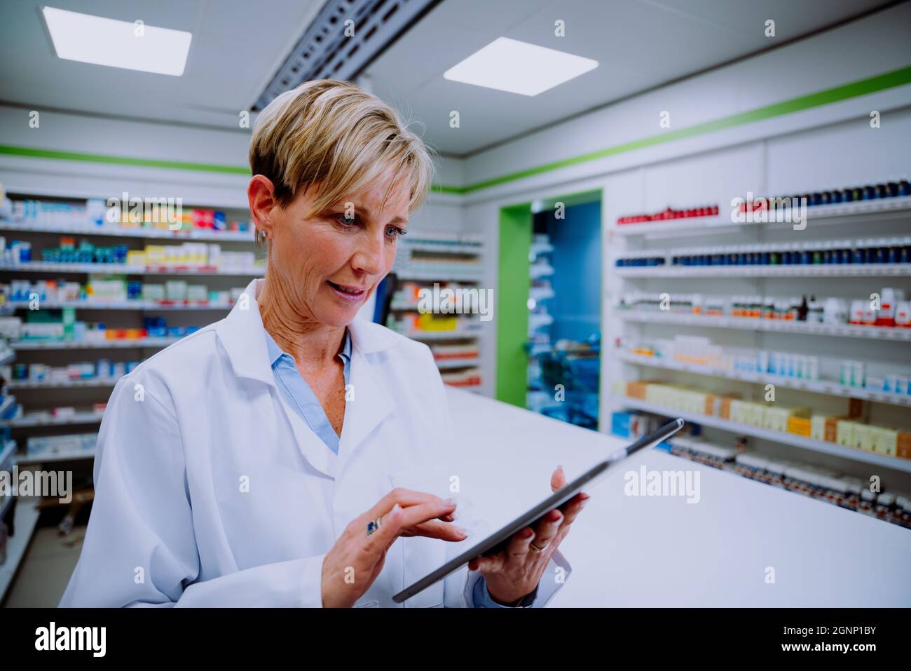 Caucasian pharmacist scrolling through digital tablet standing behind ...