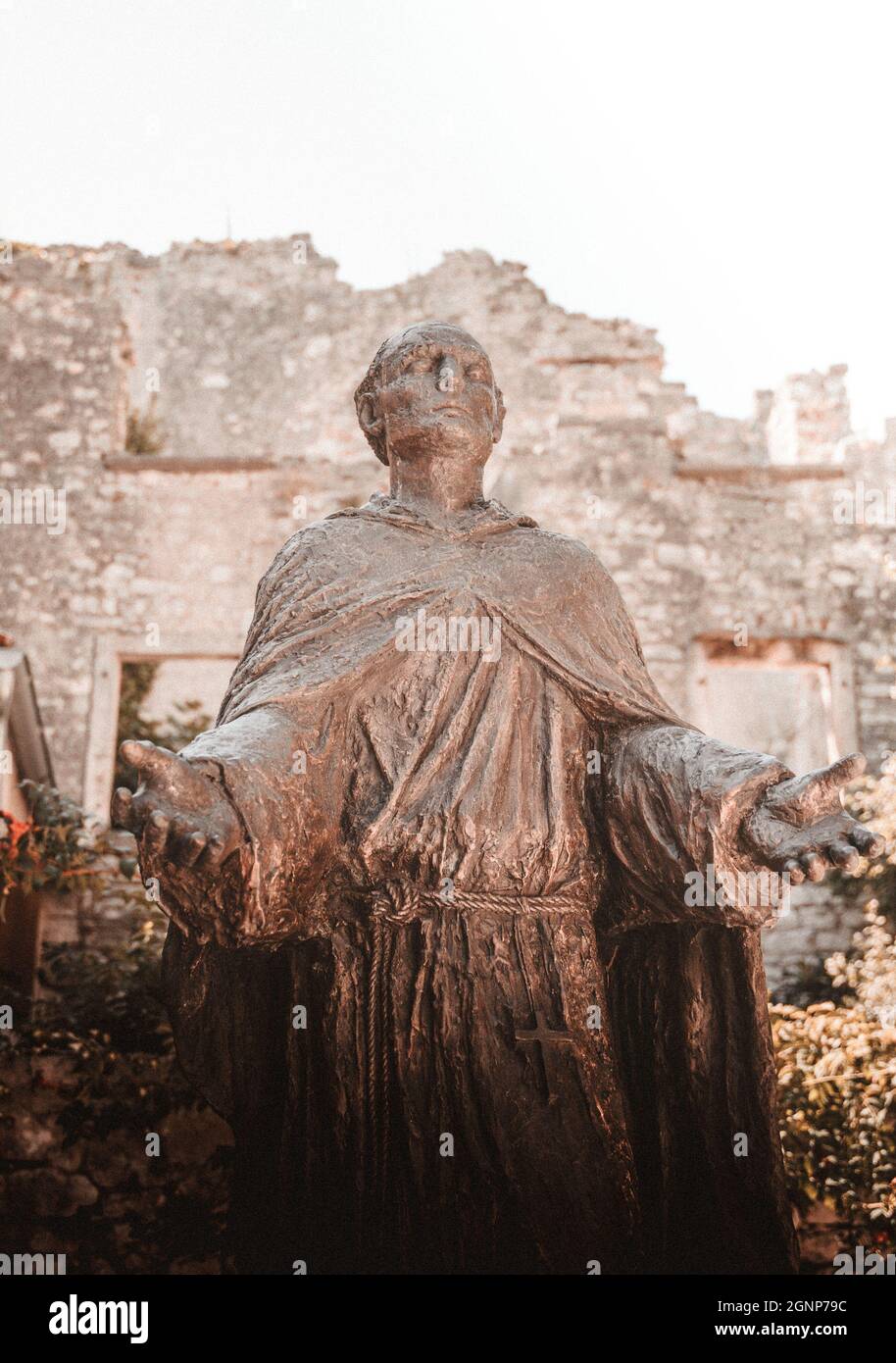 Vertical shot of a statue of a praying monk with extended hands in the ...