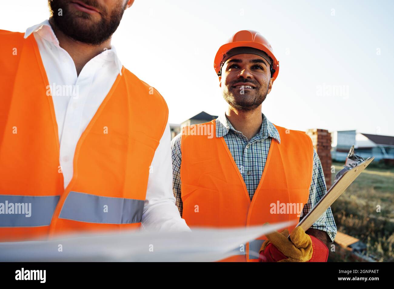 Two young male engineers in uniform and hardhats working at ...