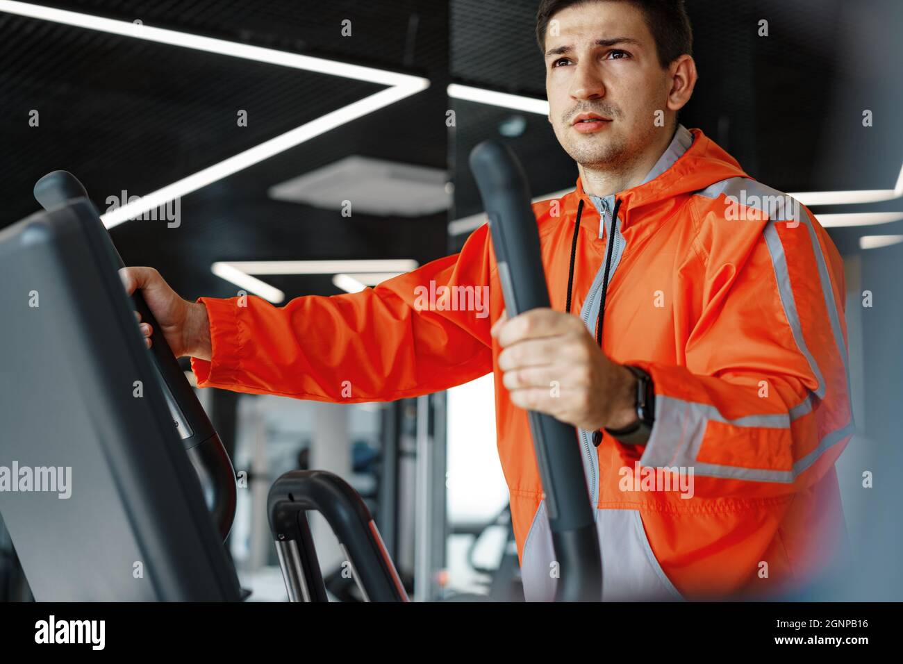 Portrait of a young man in orange windbreaker workout on a fitness ...
