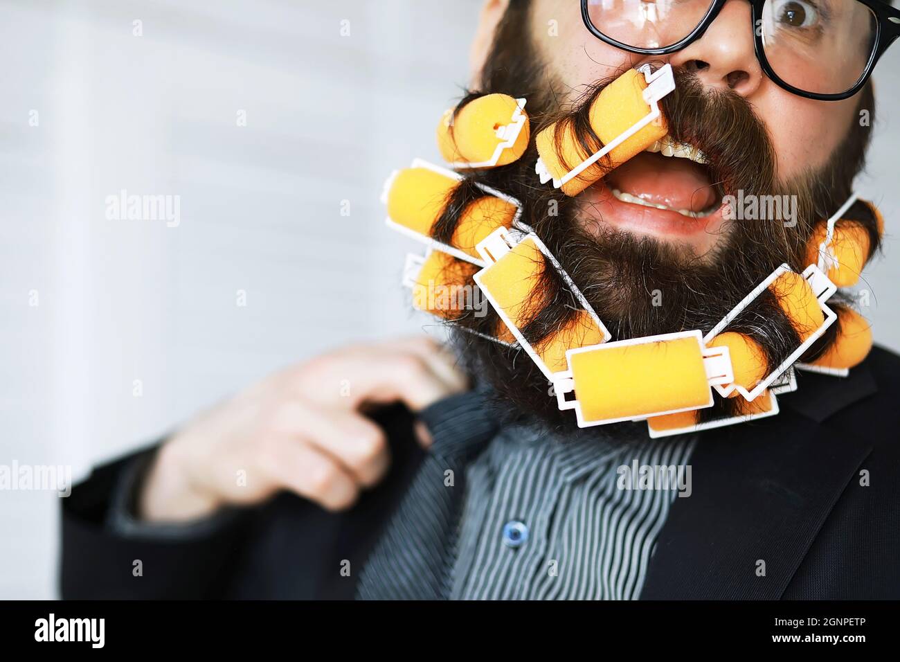 Cheerful hipster man with curlers in beard. Surprised man with glasses ...