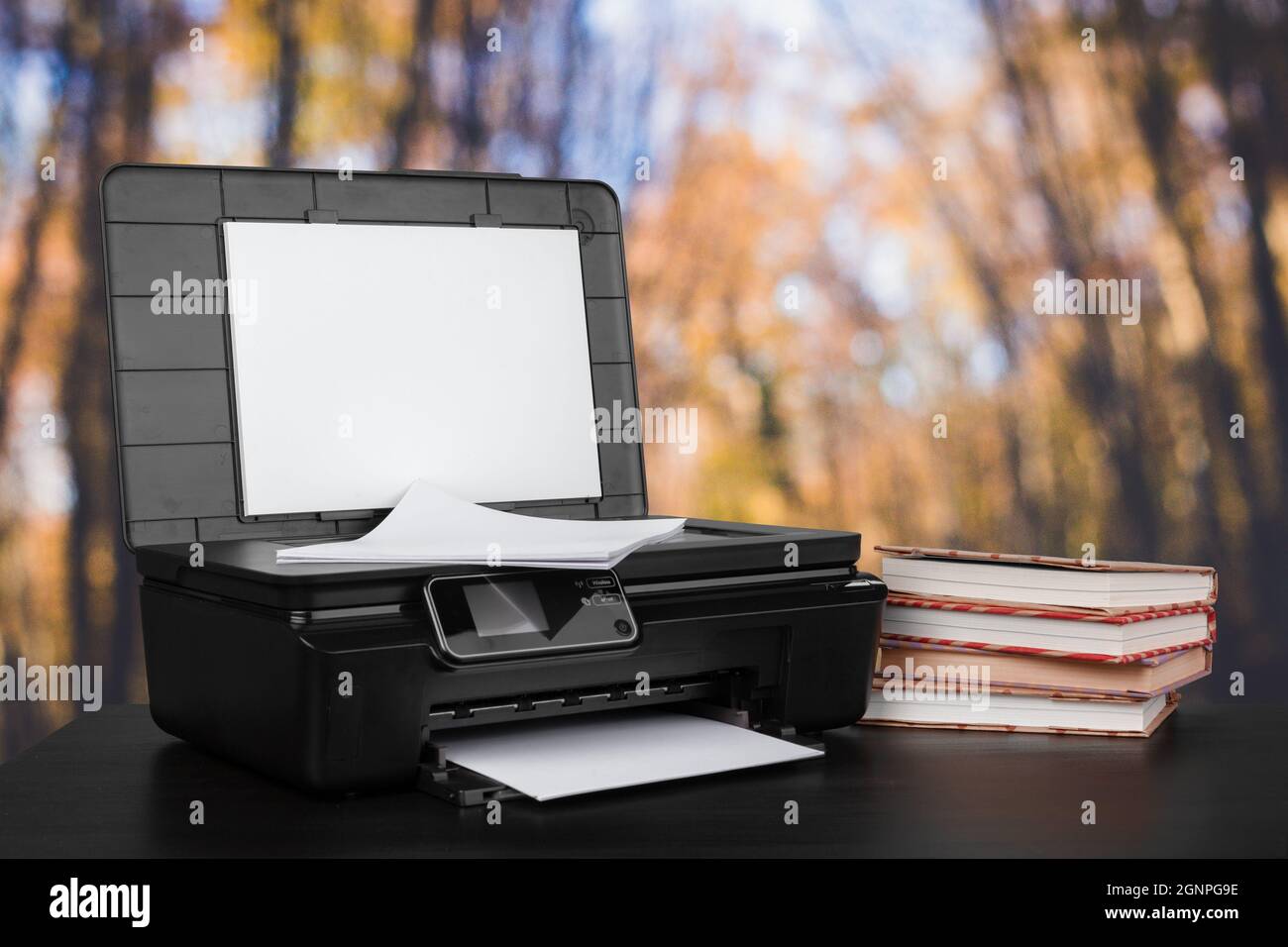 Compact home printer on desk with books against blurred background ...