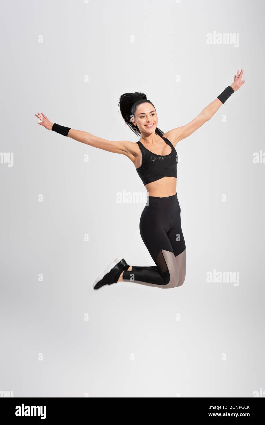 full length of happy young woman levitating with outstretched hands on ...