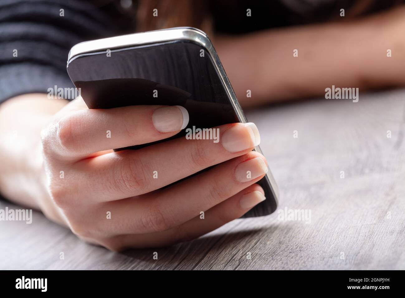 smartphone supported in one hand on a dark wood surface viewed from the ...