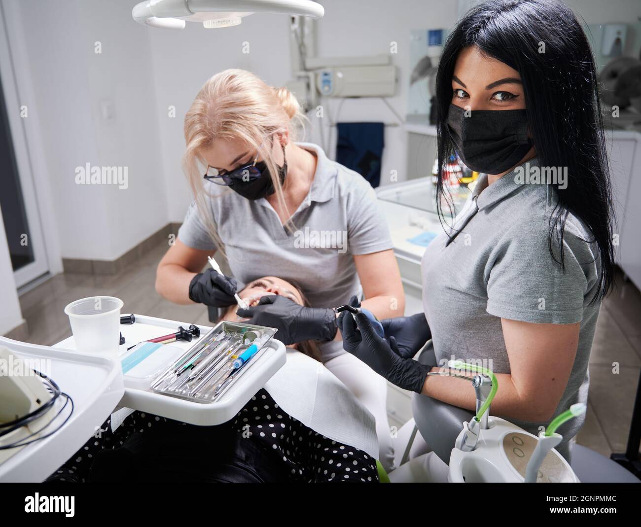 Female assistant in medical mask looking at camera while doctor ...