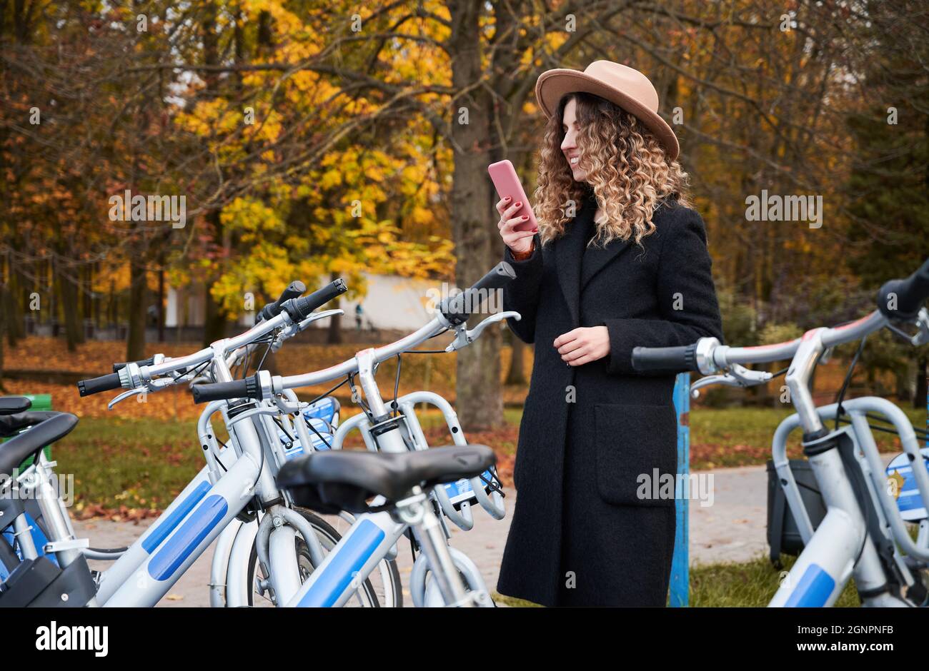 Side view of curly woman holding smartphone and scaning QR code to rent ...
